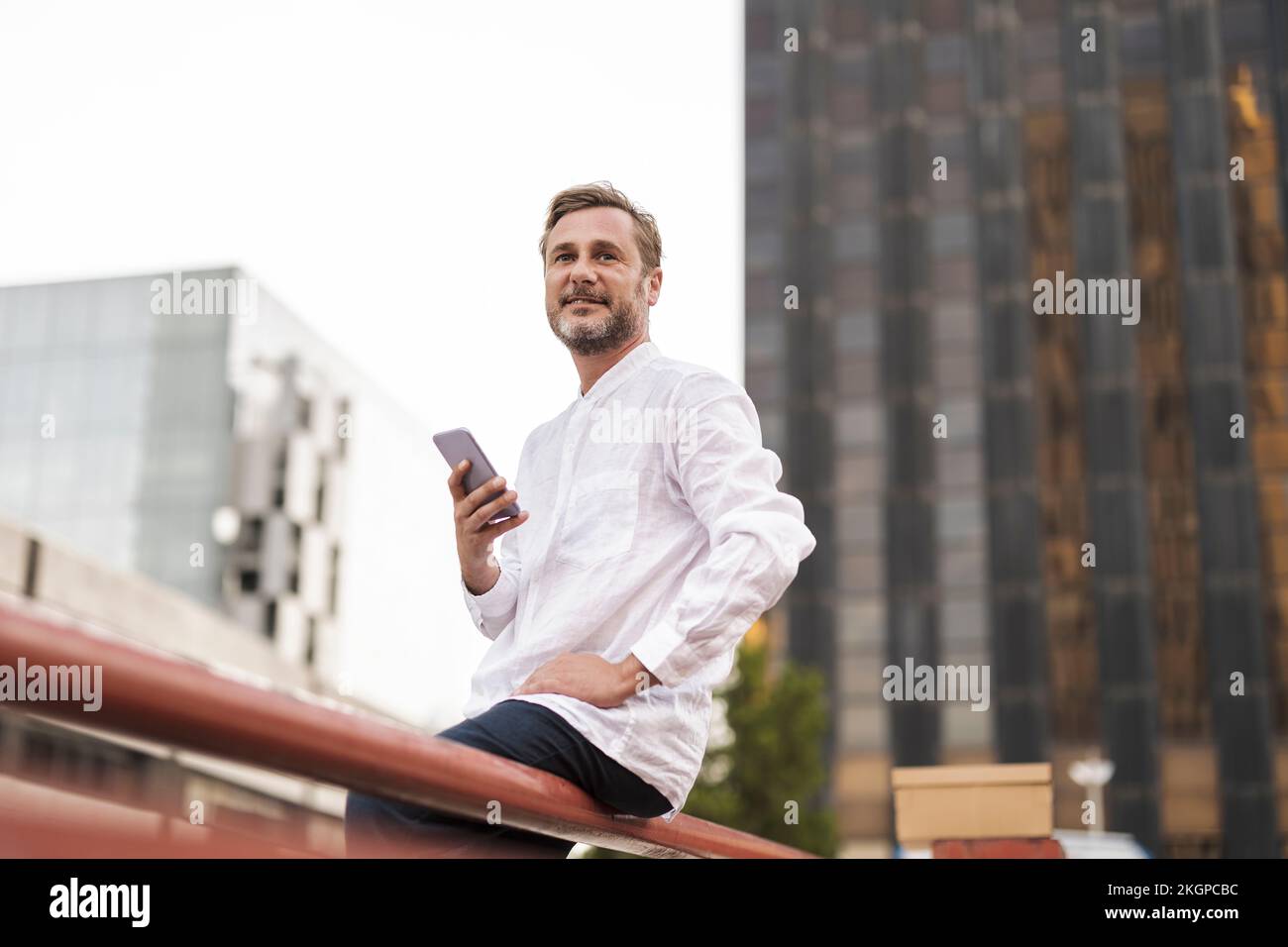 Smiling man sitting with smart phone on railing Stock Photo - Alamy
