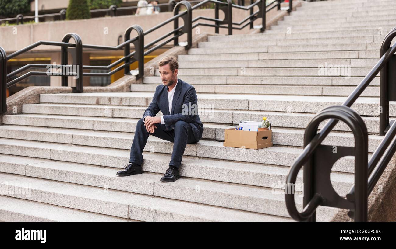 Businessman sitting with cardboard box on steps Stock Photo - Alamy