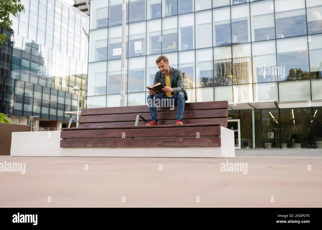 Man sitting on bench and reading book Stock Photo - Alamy