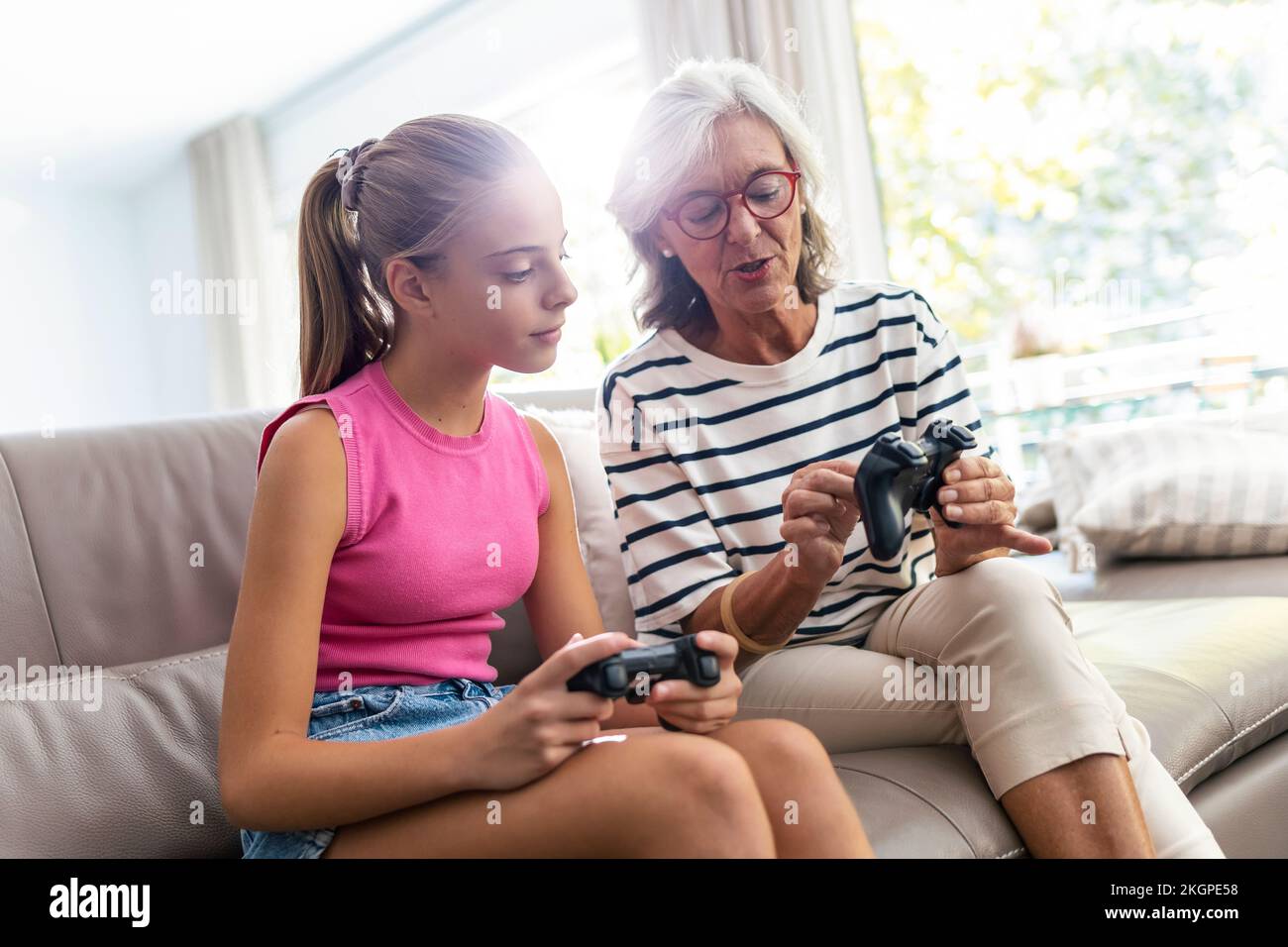 Grandmother showing game controller to granddaughter sitting on sofa at ...