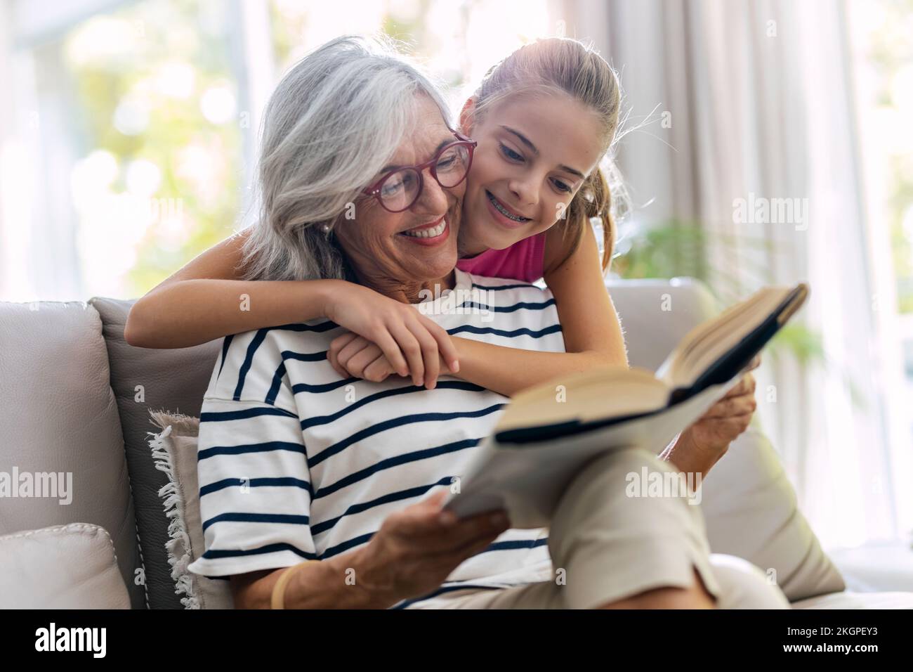 Grandmother reading book with granddaughter on sofa at home Stock Photo ...