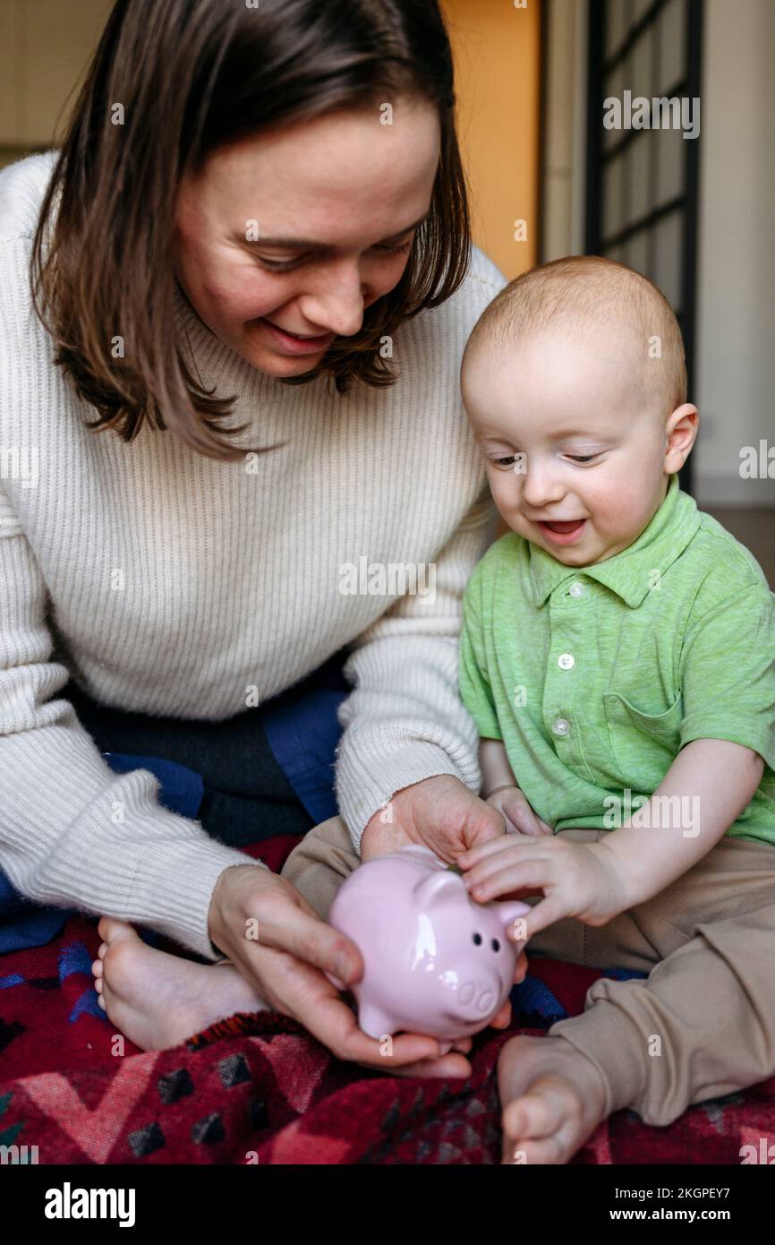Mother assisting son putting coin in piggy bank Stock Photo - Alamy