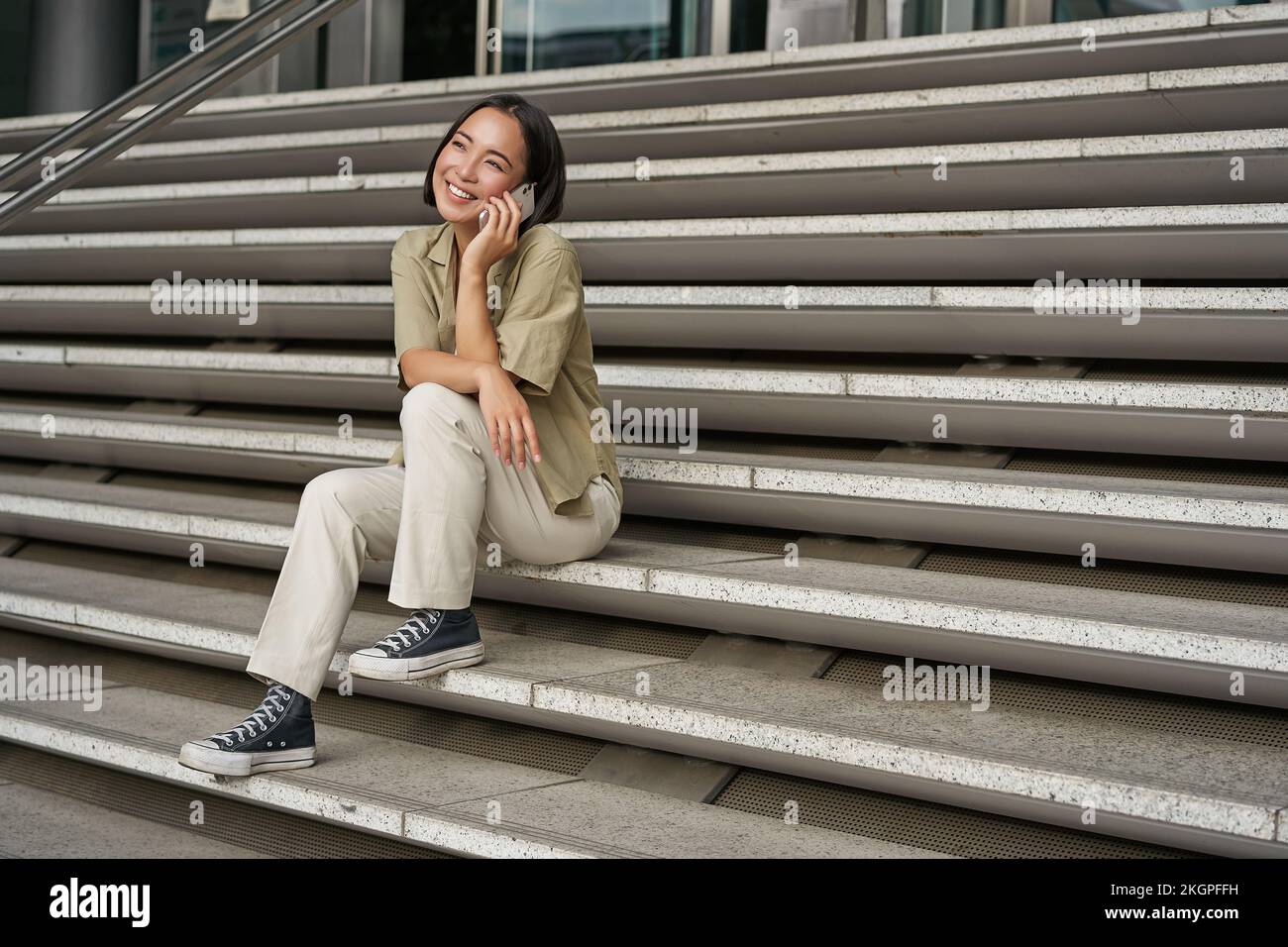 Portrait of asian student girl on stairs talks on mobile phone, smiles ...