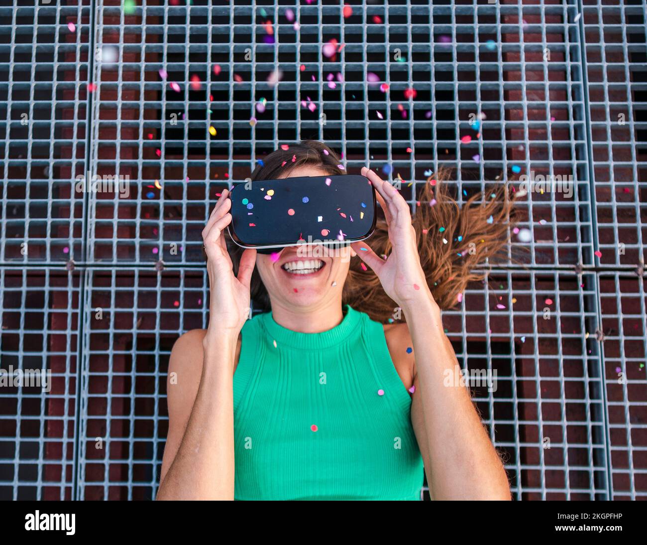 Happy woman wearing virtual reality glasses lying on metal footpath ...