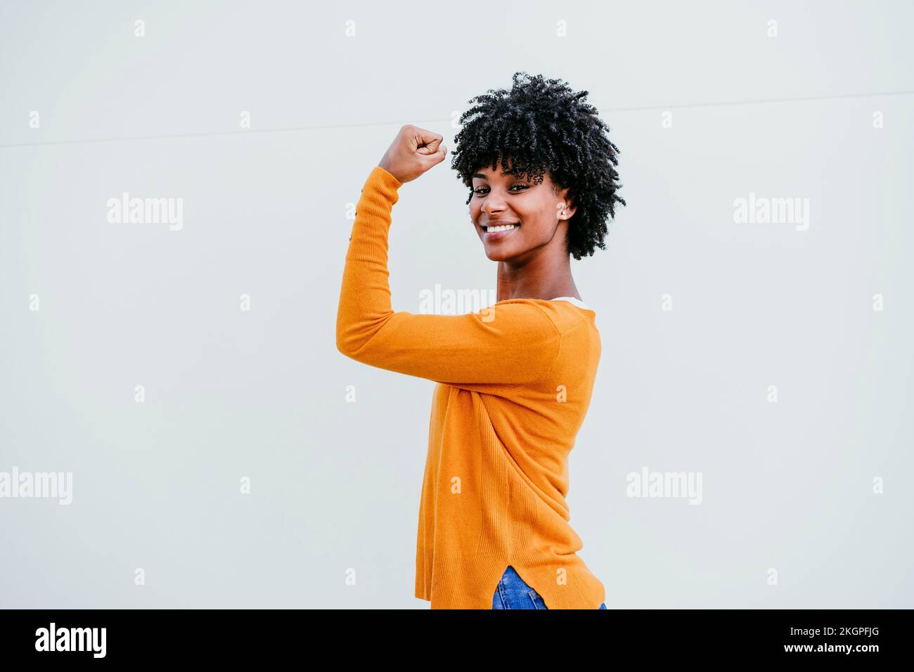 Smiling young woman flexing muscle near white wall Stock Photo - Alamy