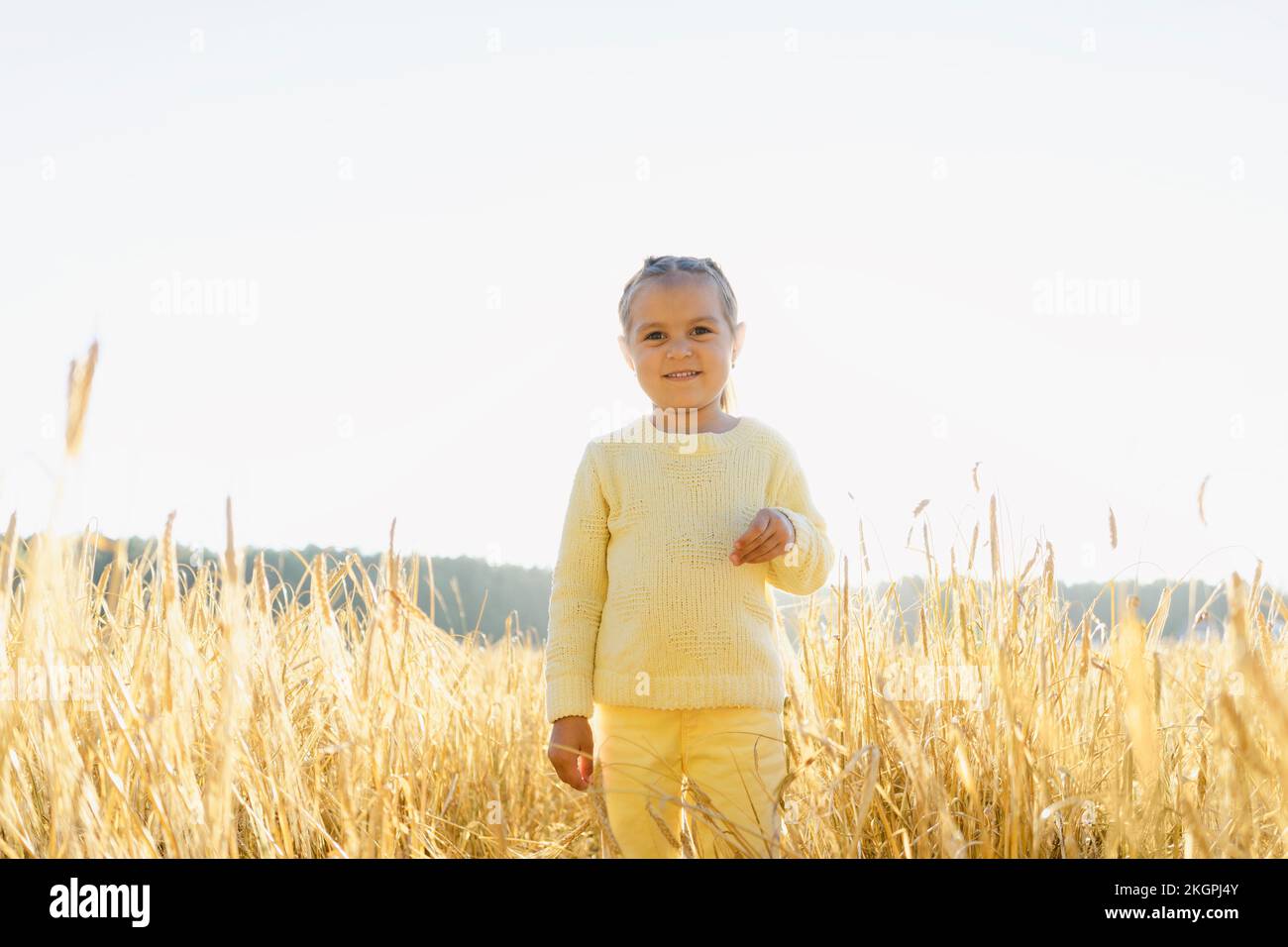 Happy cute girl standing amidst crops at field in front of clear sky ...