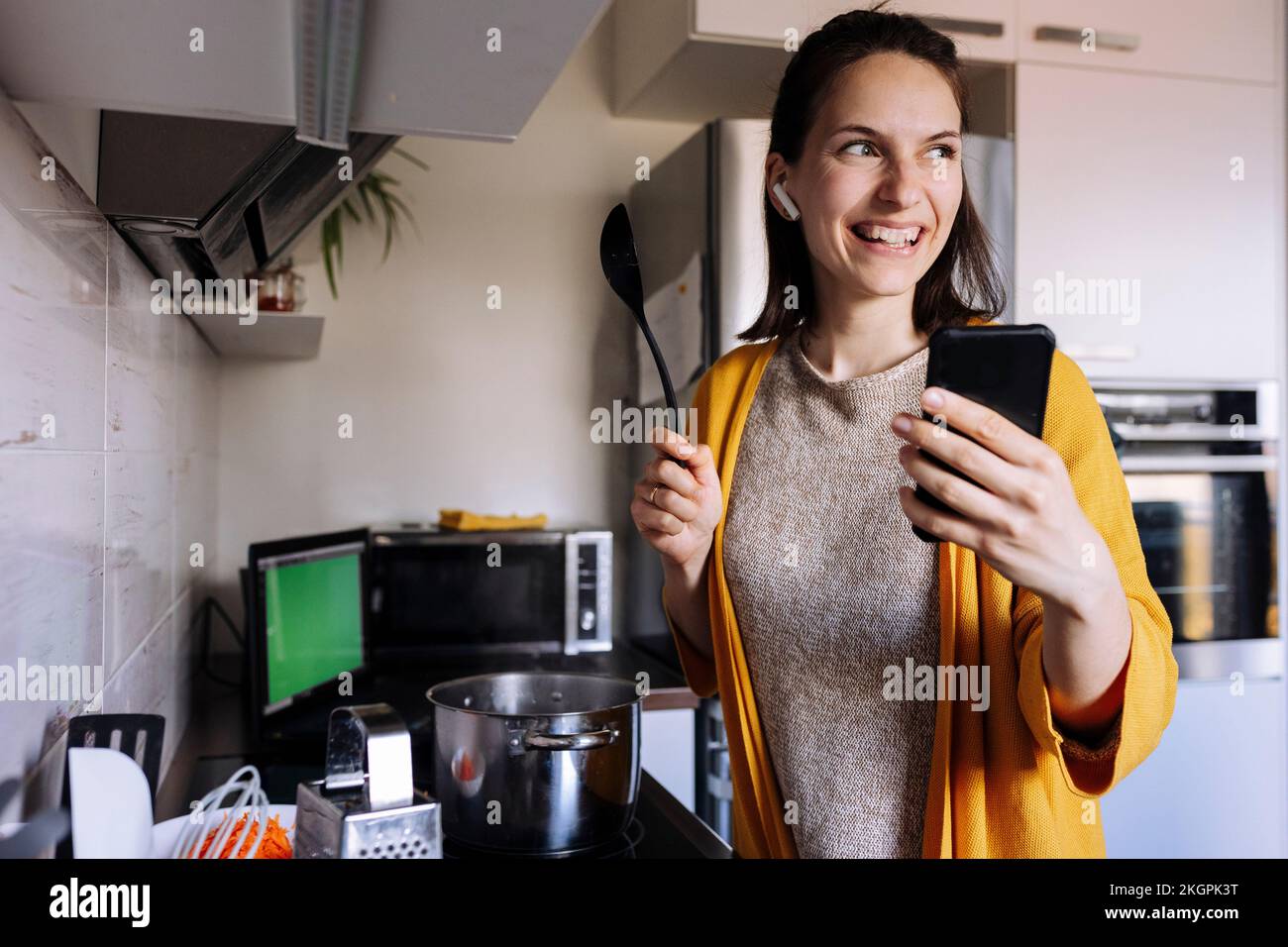 Happy young woman cooking and having video call through smart phone in ...