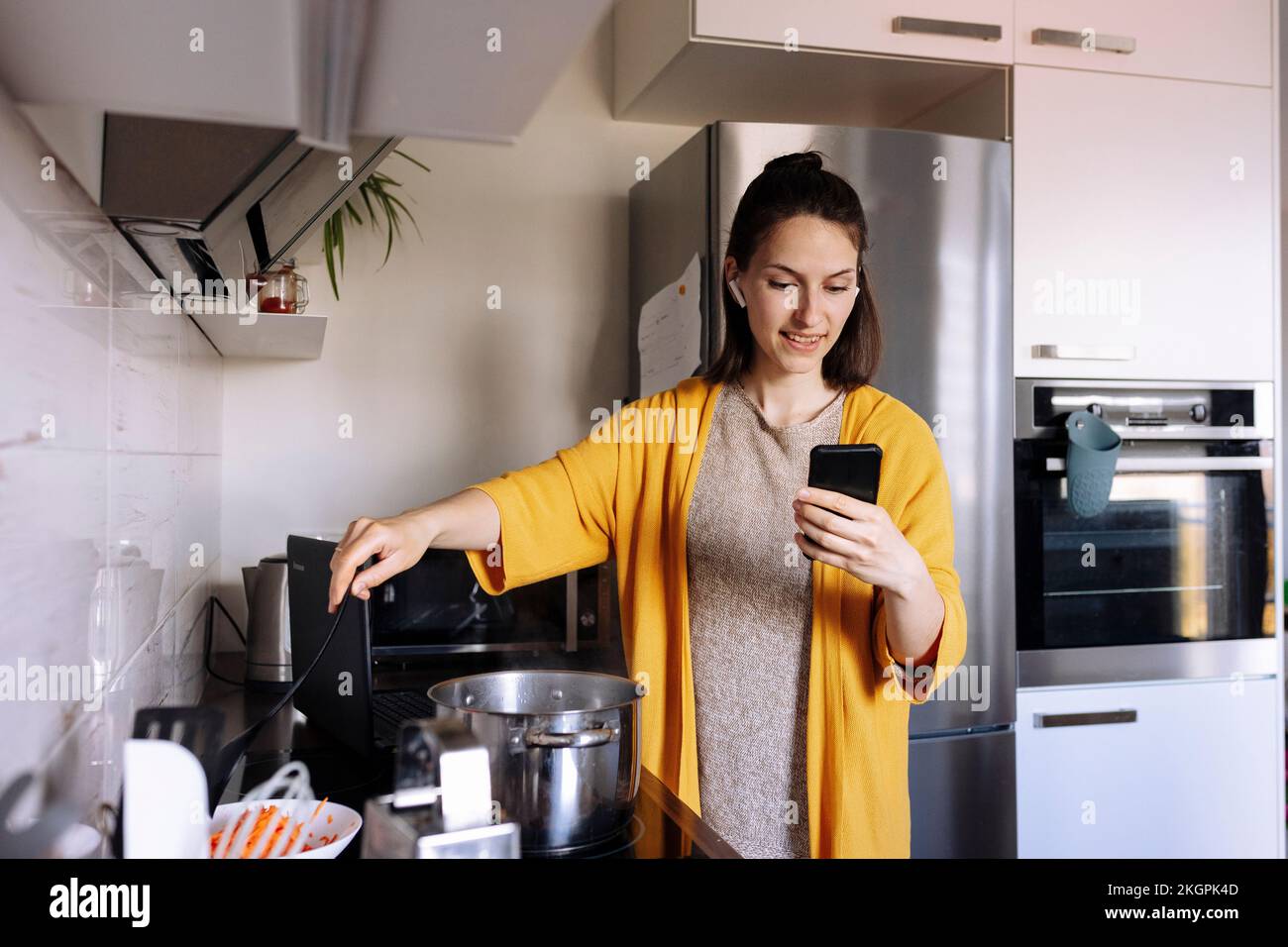 Woman cooking and having video call through smart phone in kitchen ...