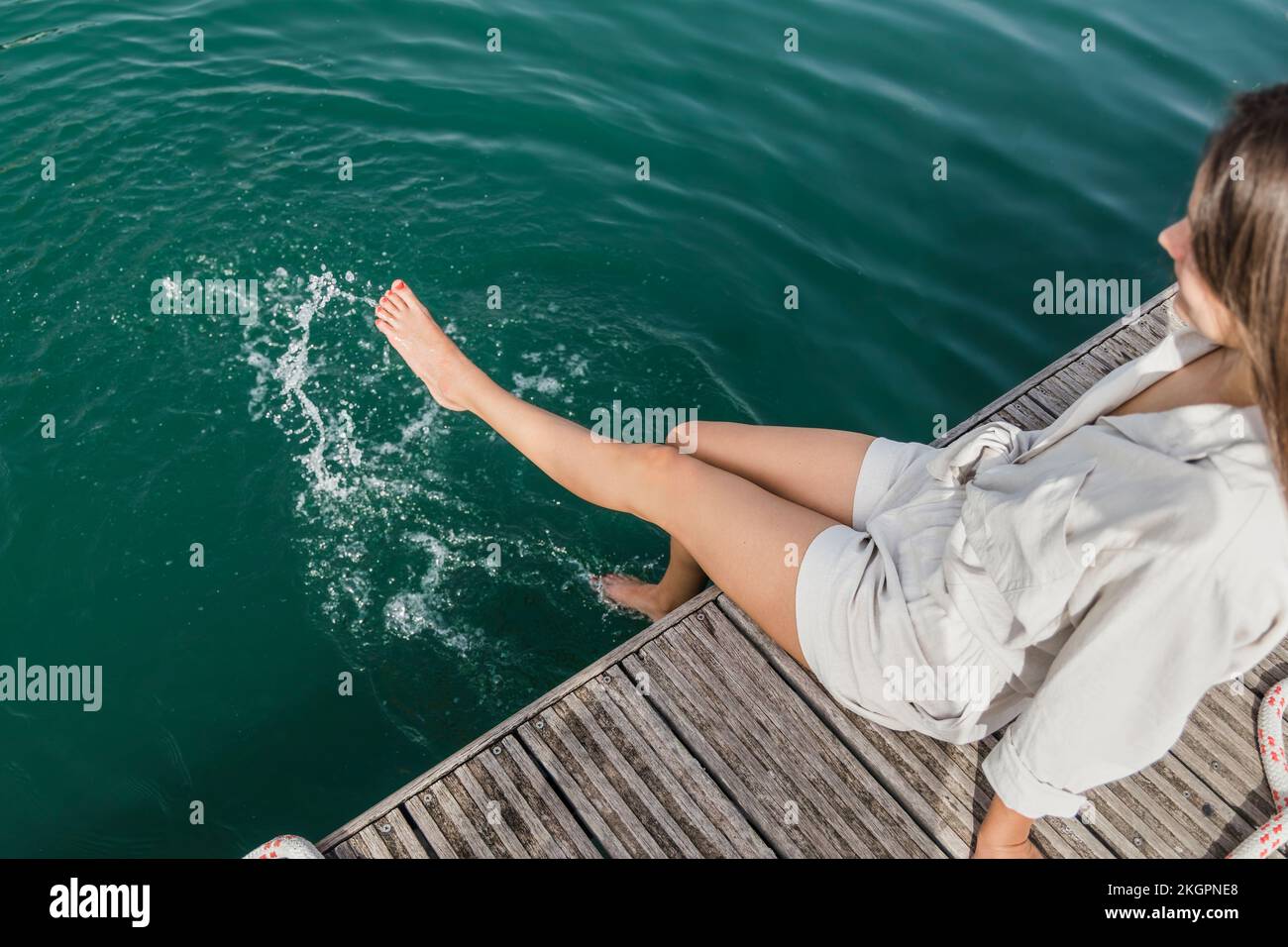 Young woman splashing feet in water at jetty Stock Photo - Alamy