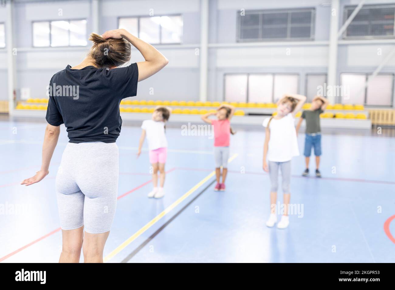 Teacher instructing students doing stretching exercises standing at ...