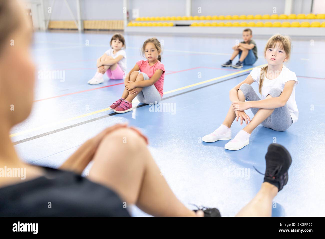 Elementary students looking at teacher teaching exercises sitting at ...