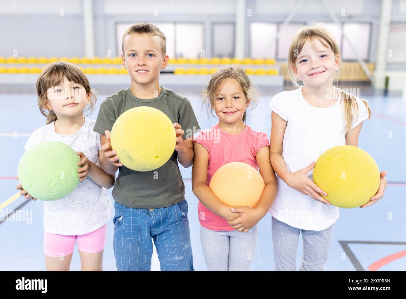 Smiling elementary students with ball standing side by side at school ...
