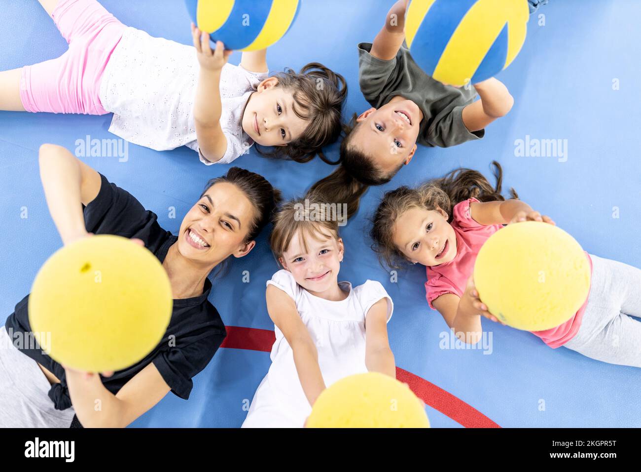 Happy students and teacher lying down with ball at school sports court ...