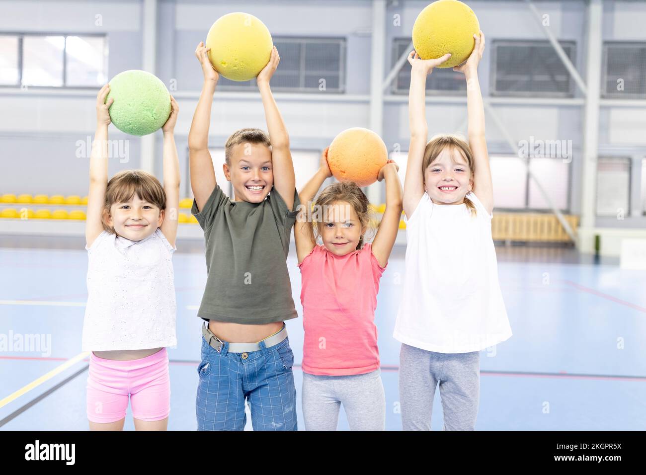 Cheerful students with arms raised holding ball standing together at ...
