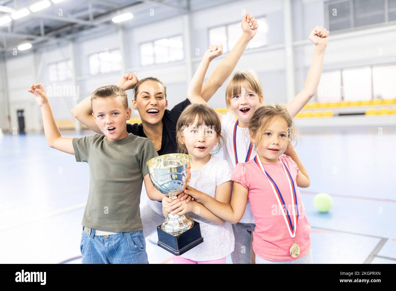 Teacher cheering with students holding trophy at school sports court ...