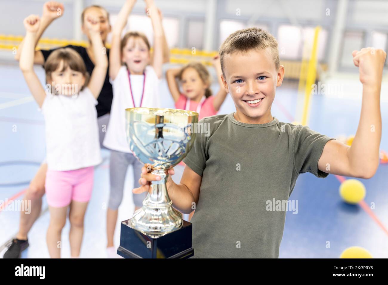 Happy boy flexing muscle holding trophy with friends at school sports ...