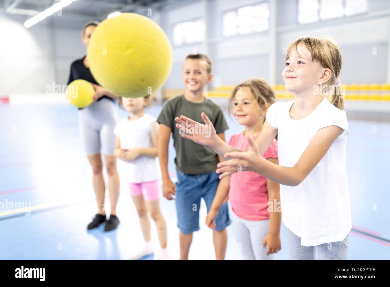 Smiling girl catching ball with friends at school sports court Stock ...