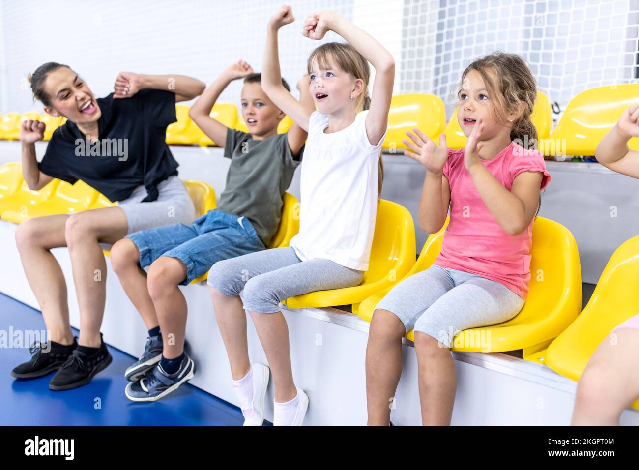 Teacher cheering with students sitting on seat at school sports court ...