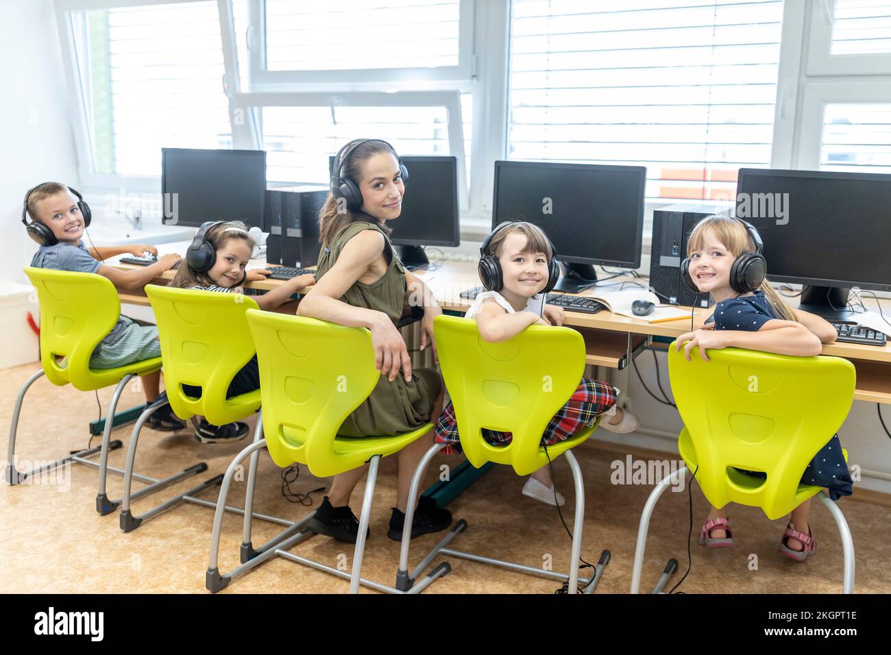 Smiling students with teacher wearing headphones sitting in computer ...