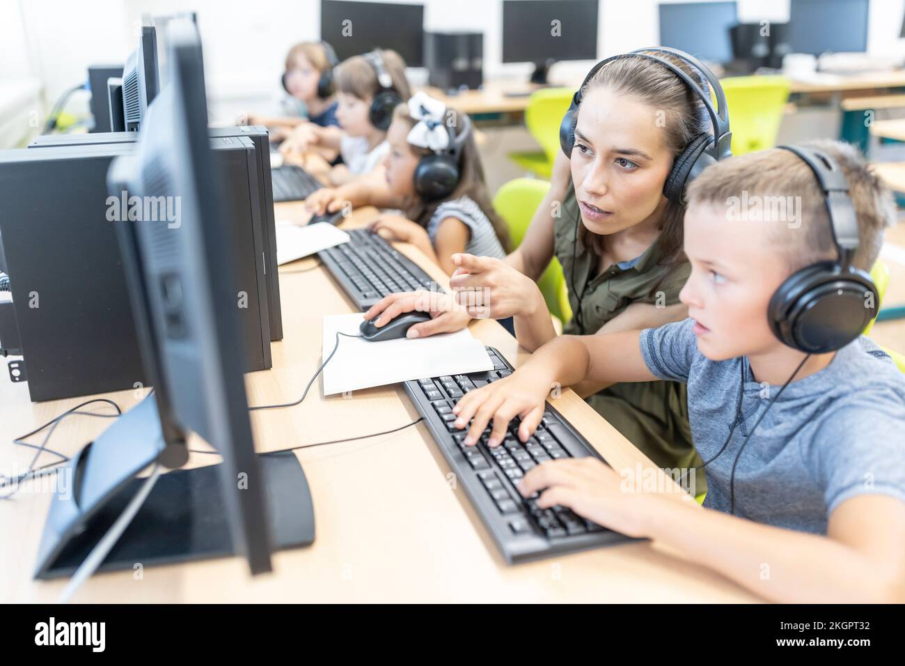 Teacher gesturing by student wearing headphones doing E-learning at ...
