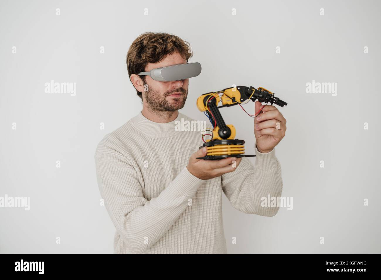 Engineer examining robotic arm wearing VR goggles in front of white ...