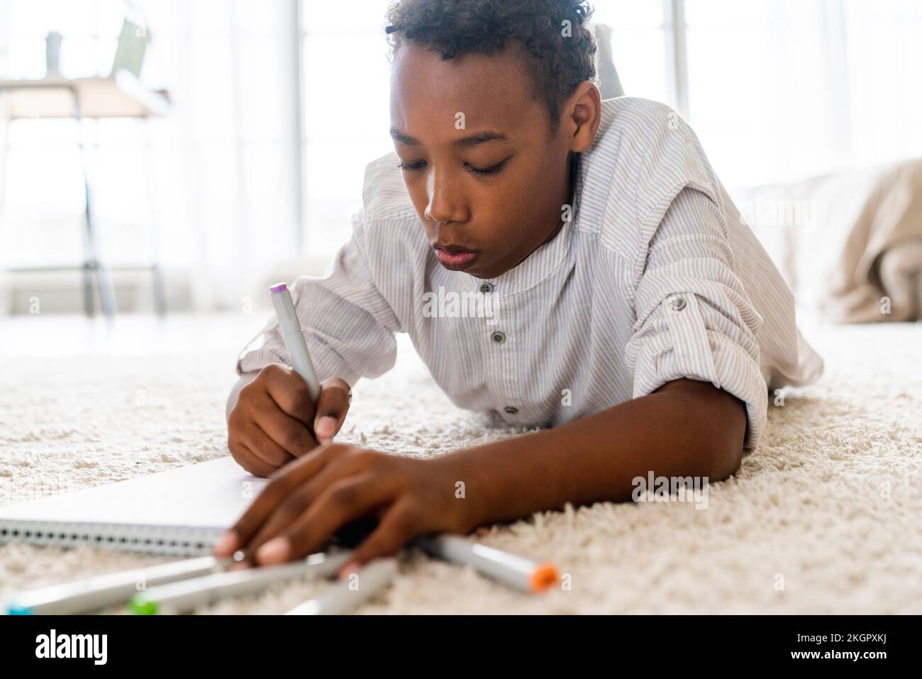 Boy with felt tip pen writing in book lying on carpet Stock Photo - Alamy