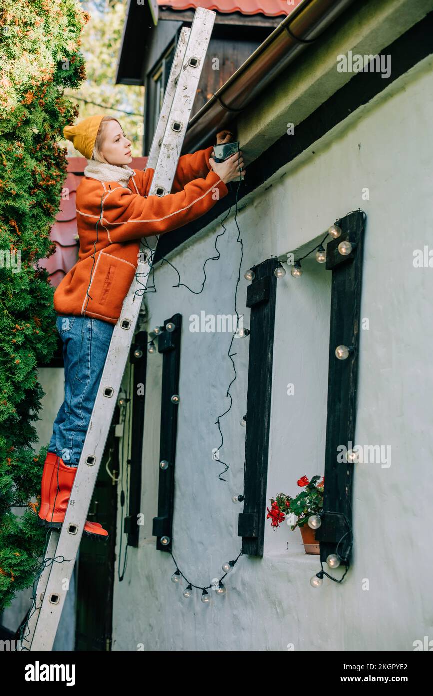 Woman decorating house with lights standing on ladder Stock Photo - Alamy