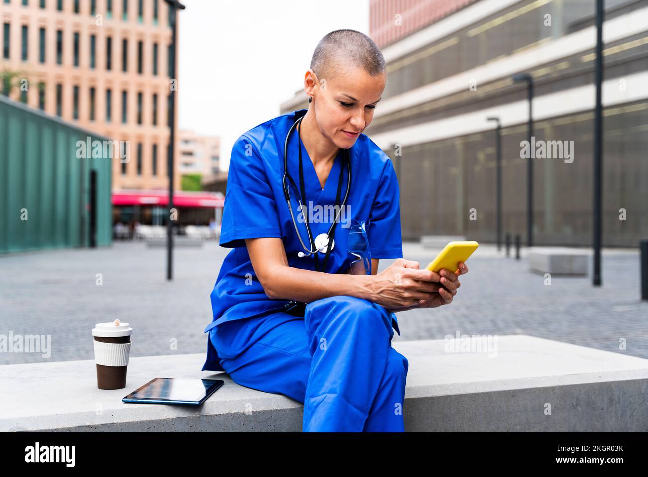 Mature female nurse using mobile phone sitting on bench Stock Photo - Alamy