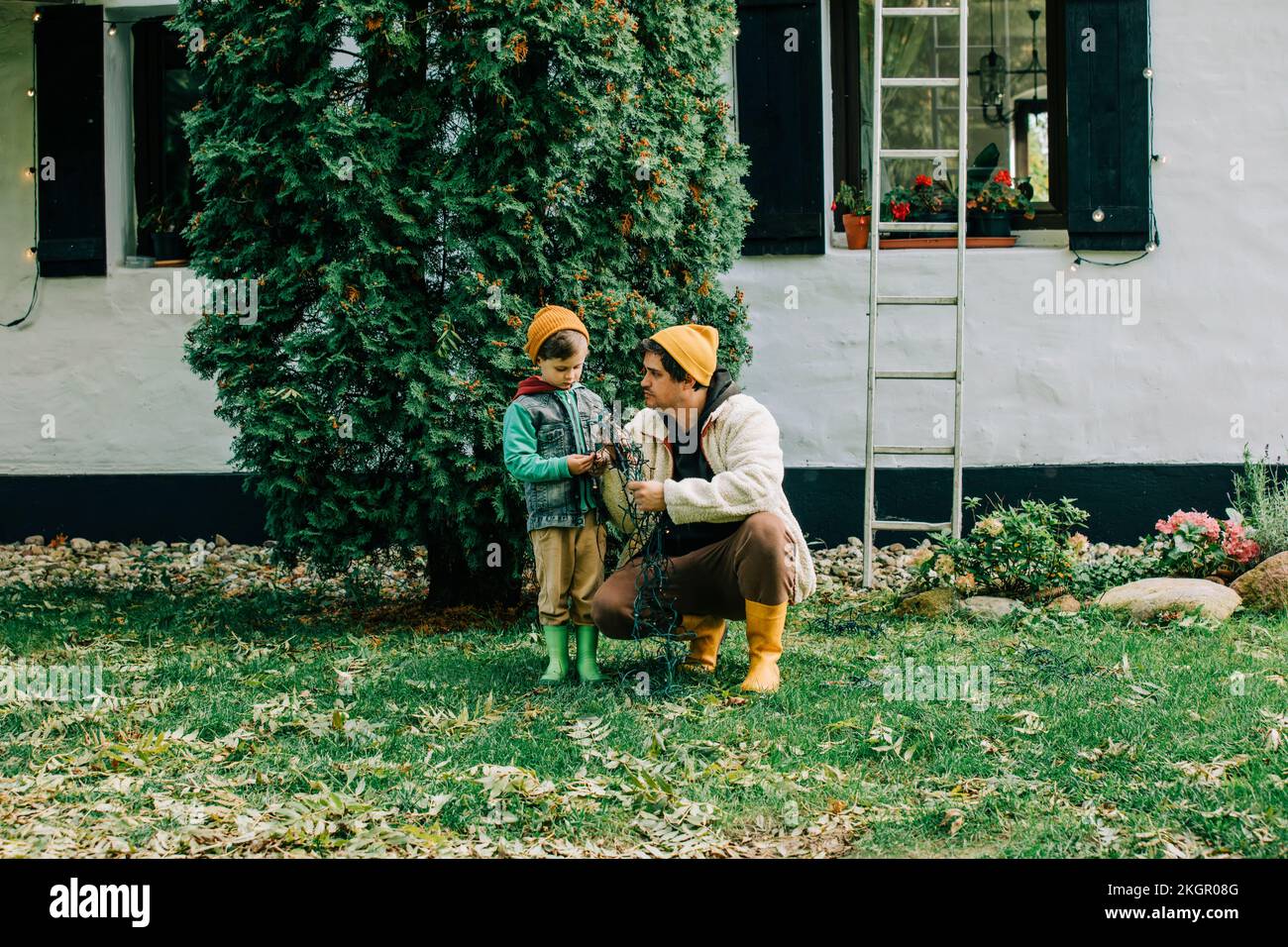 Father crouching by son in front of tree outside house Stock Photo - Alamy