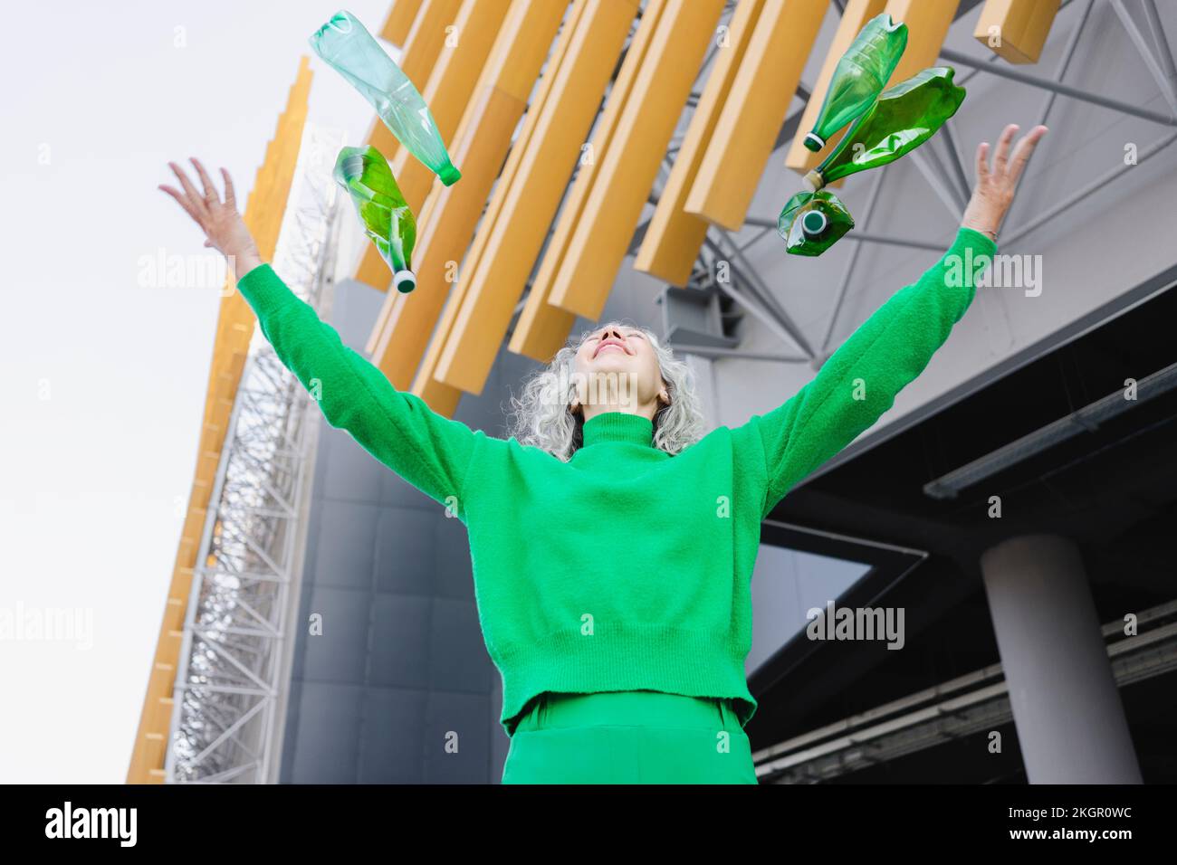 Woman with arms raised throwing plastic bottles in front of building ...