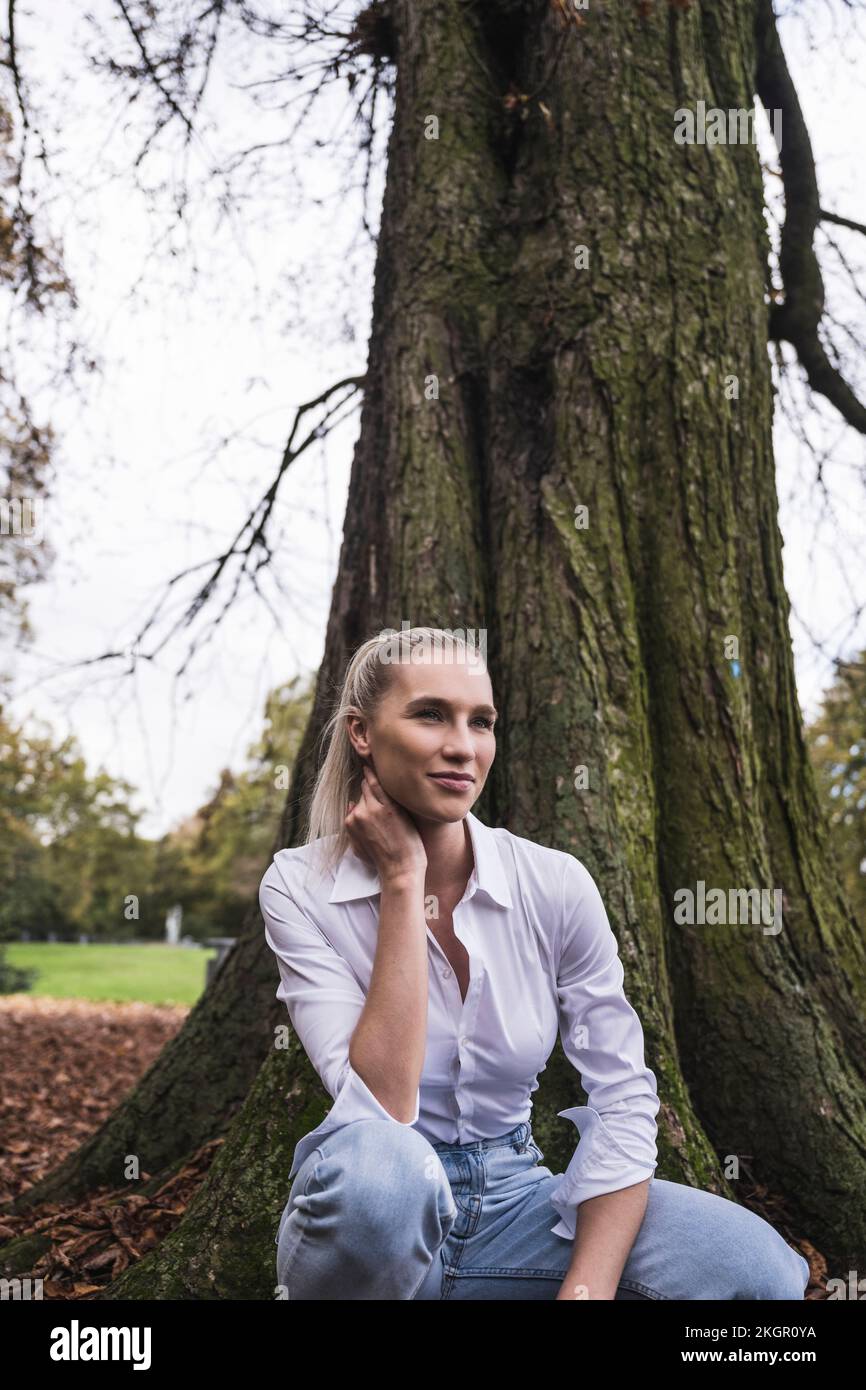 Thoughtful woman crouching in front of tree at park Stock Photo - Alamy