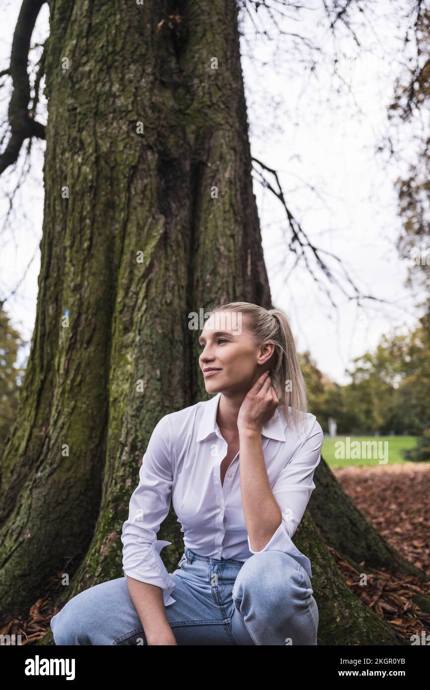 Young woman crouching in front of tree at park Stock Photo - Alamy
