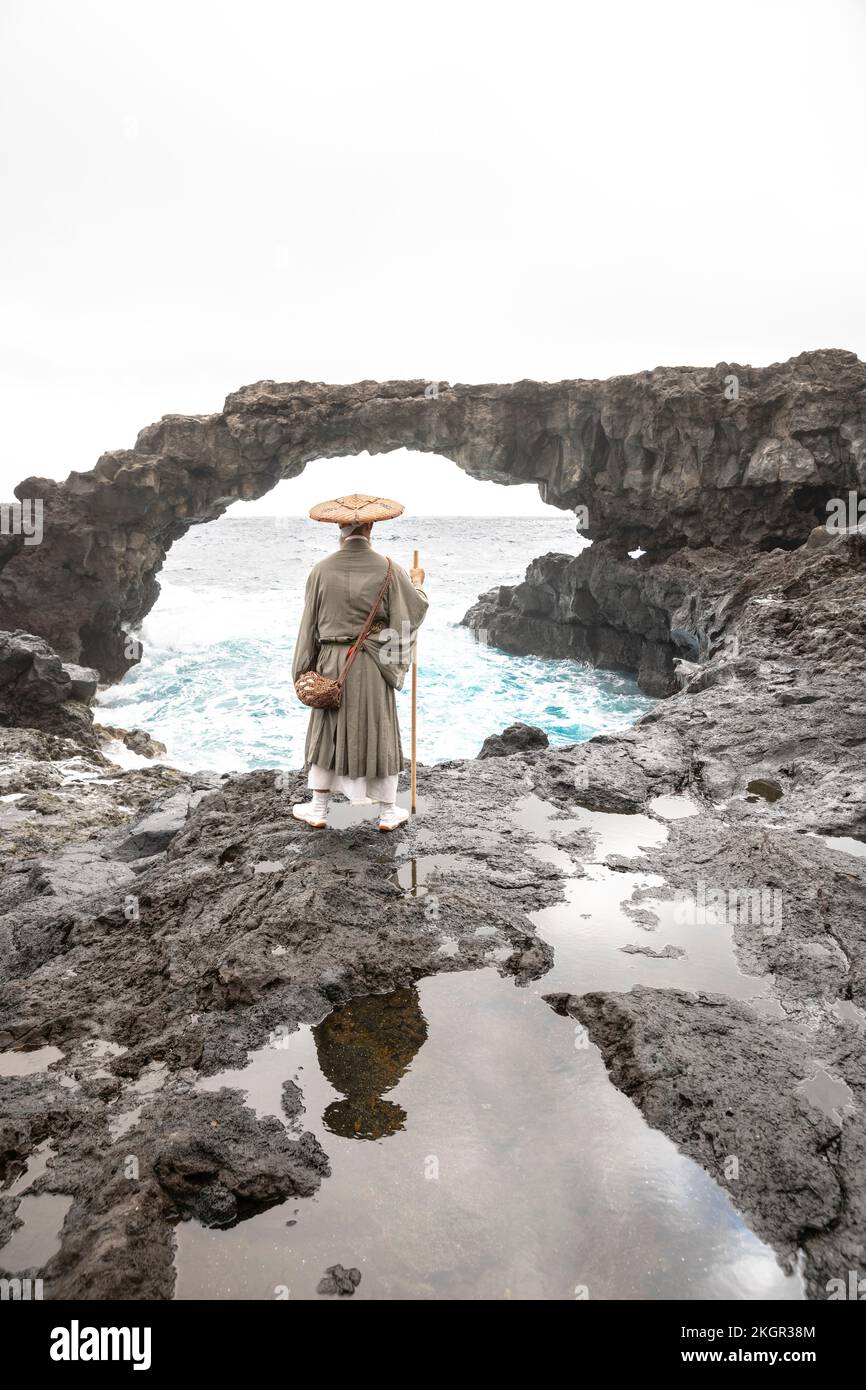 Mature monk with stick standing in front of rock arch Stock Photo - Alamy