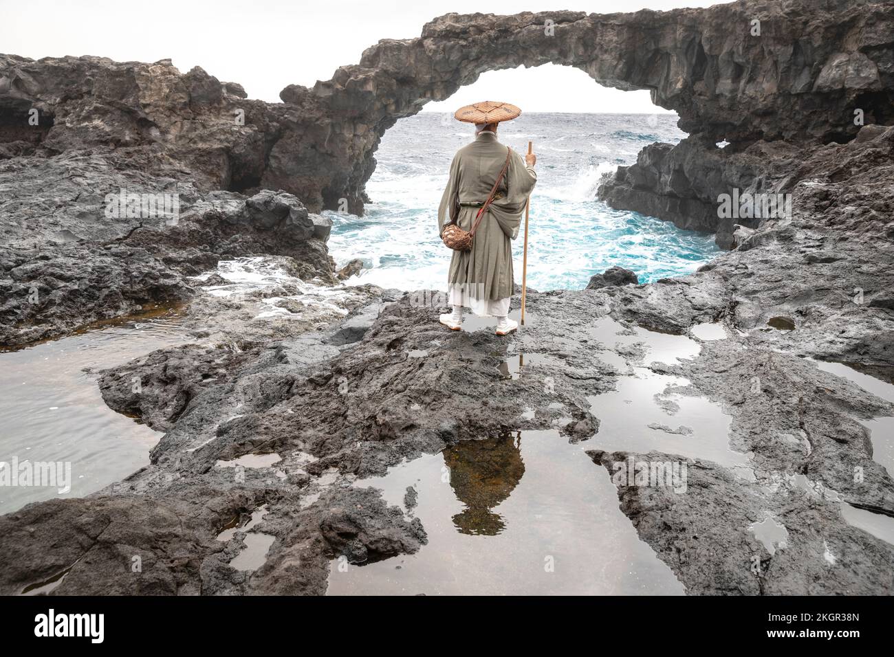 Monk with stick standing in front of rock arch Stock Photo - Alamy