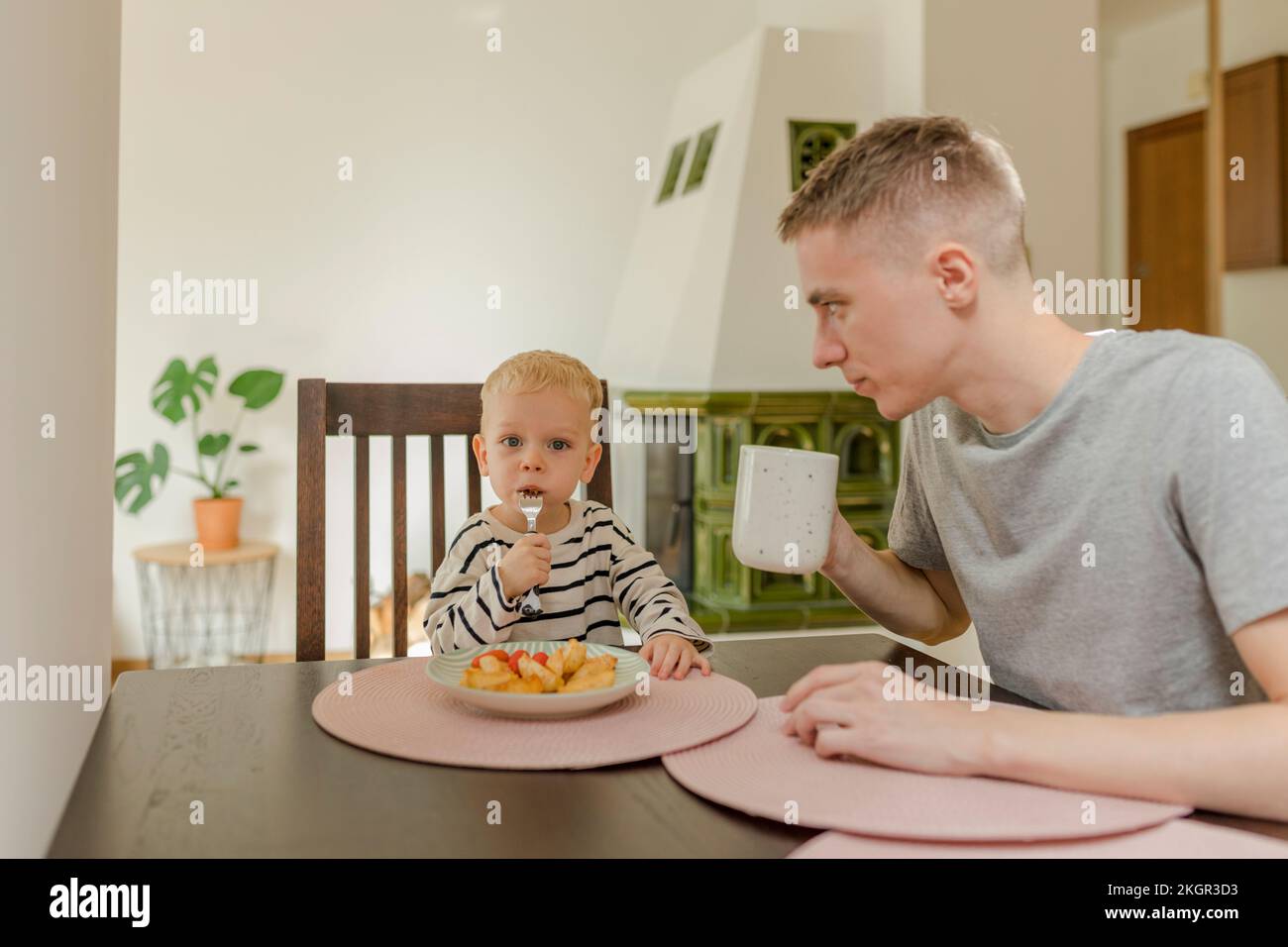 Cute boy eating food with father holding tea cup at dining table Stock ...