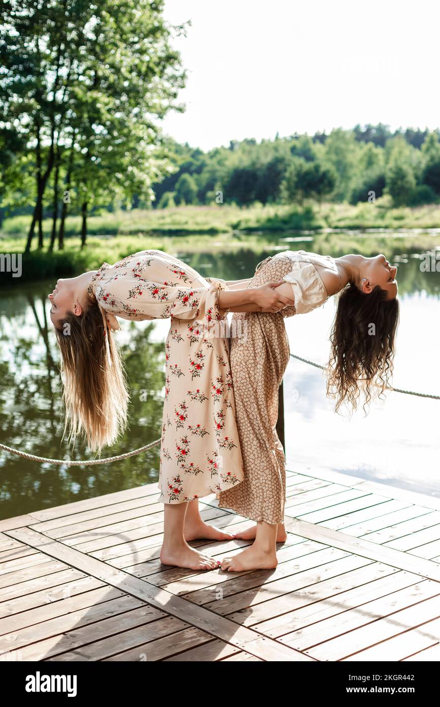 Young friends bending over backwards by holding each other on pier ...