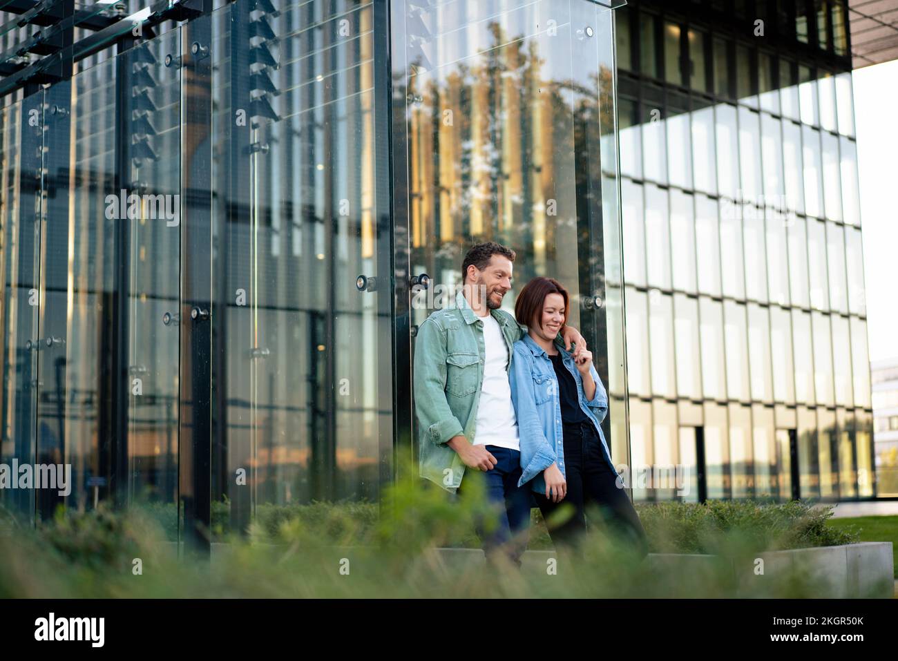 Happy couple leaning on building's glass wall Stock Photo - Alamy