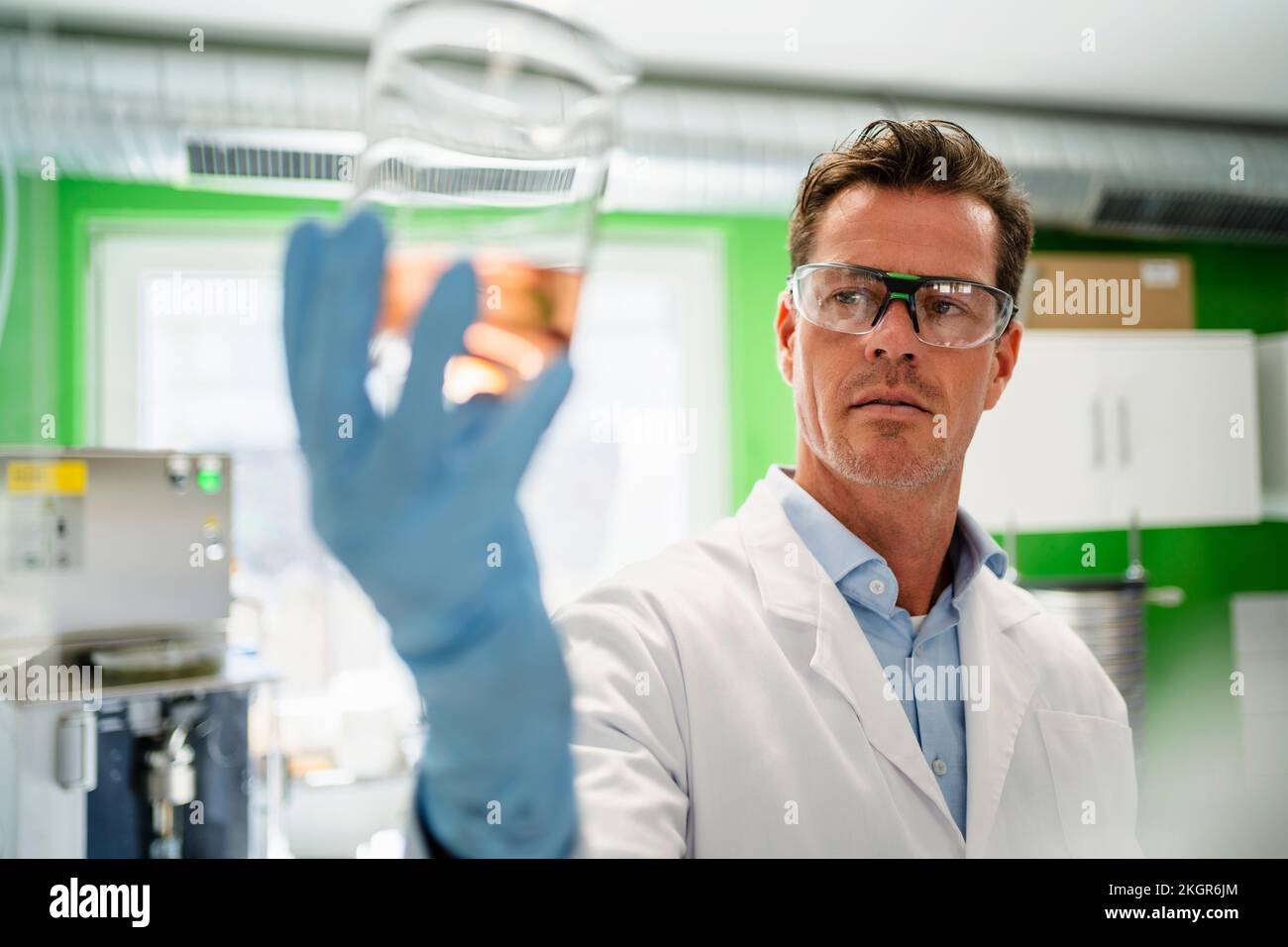 Scientist wearing eyeglasses examining measuring beaker at laboratory ...
