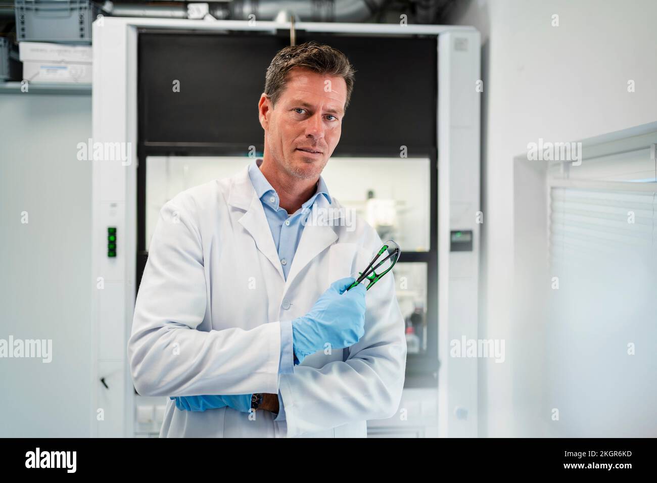 Scientist in lab coat holding eyeglasses standing at laboratory Stock ...