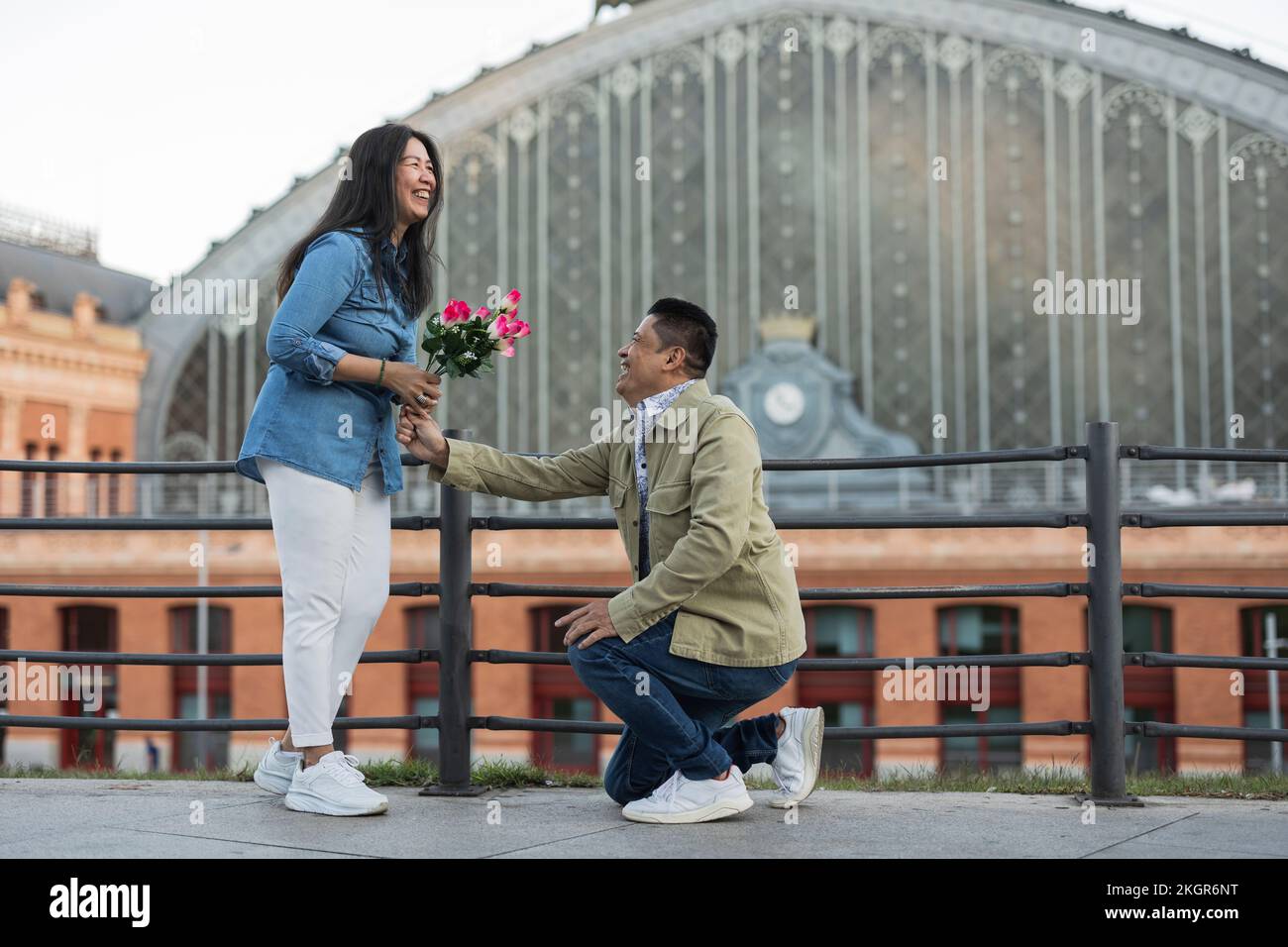 Happy man giving flowers to woman and proposing at footpath on Valentine's day Stock Photo - Alamy