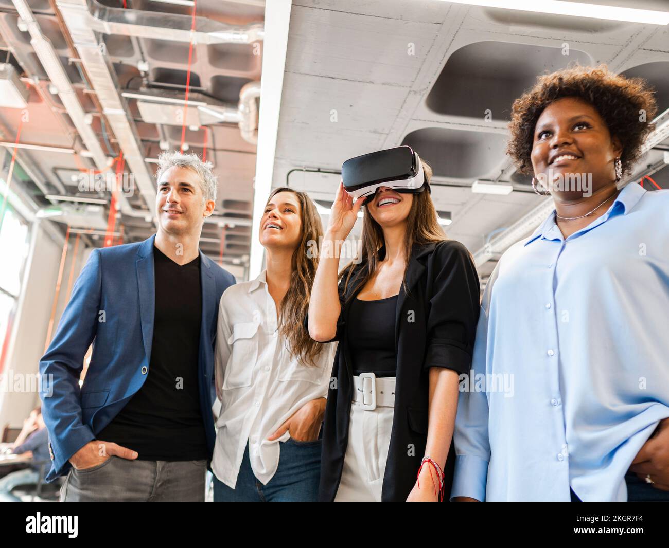 Happy businesswoman wearing VR goggles standing with colleagues in ...