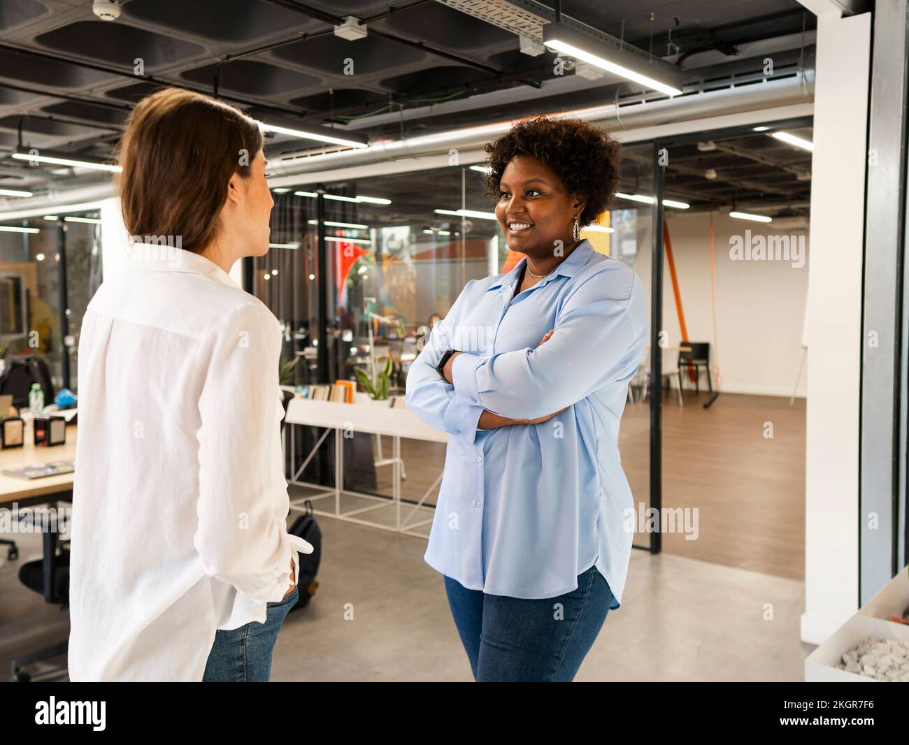 Businesswoman with arms crossed talking with colleague in office Stock ...