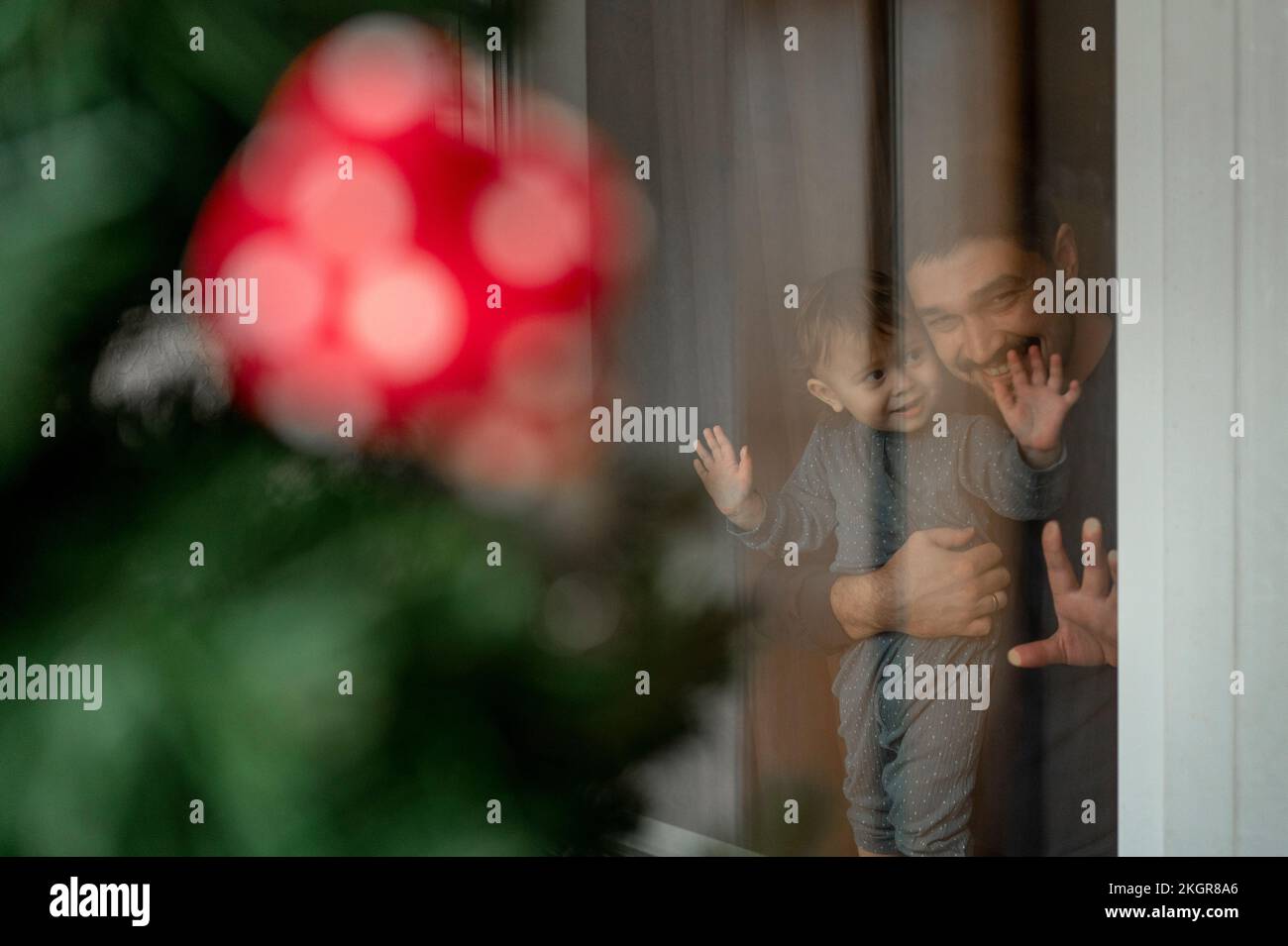 Father and son looking out of window at Christmas tree in home Stock ...