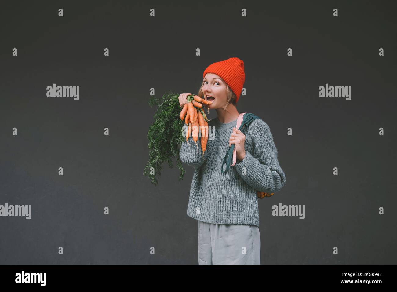 Woman eating carrots in front of gray wall Stock Photo - Alamy