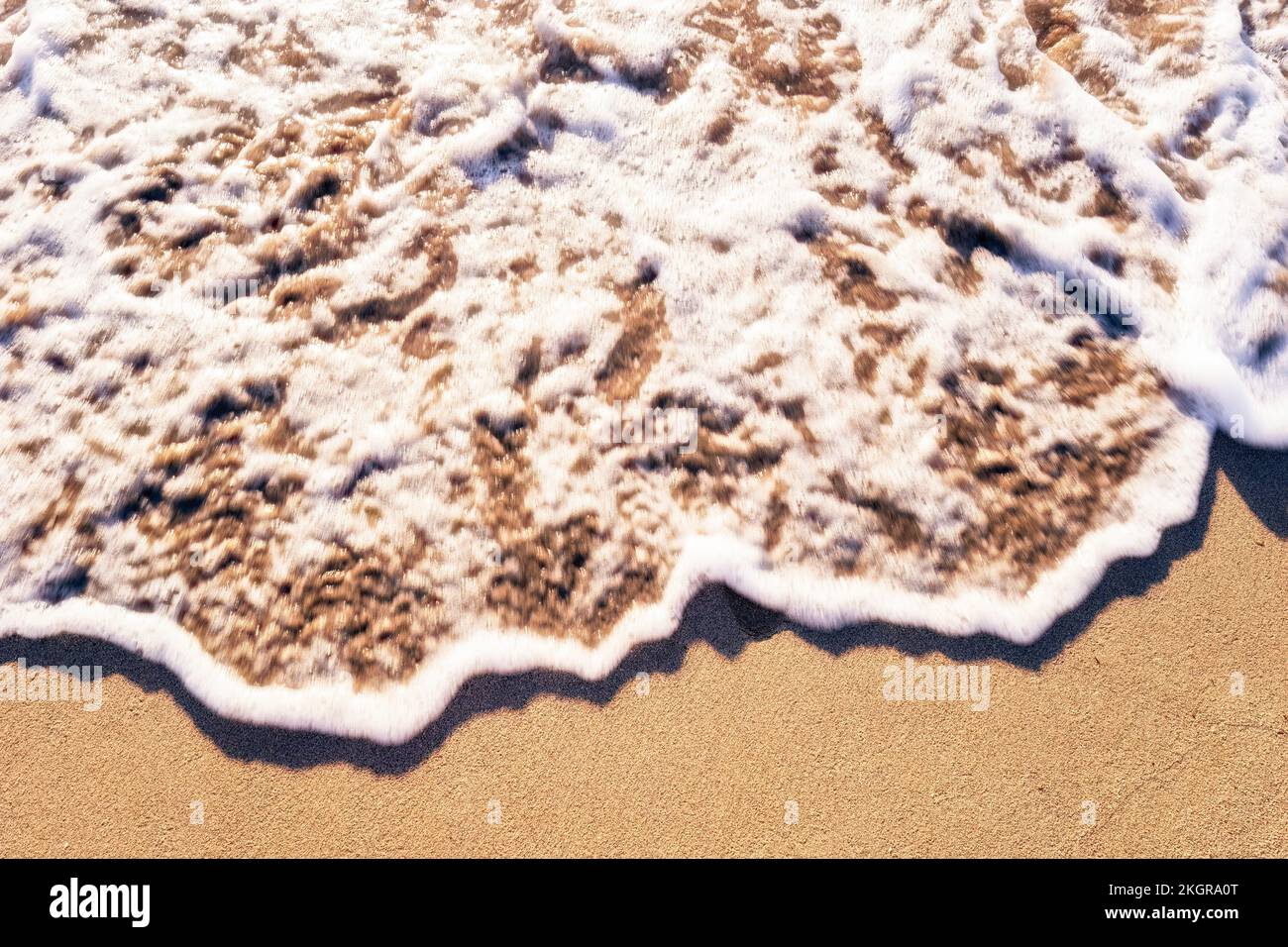 Beach sand brushed by foamy wave Stock Photo - Alamy