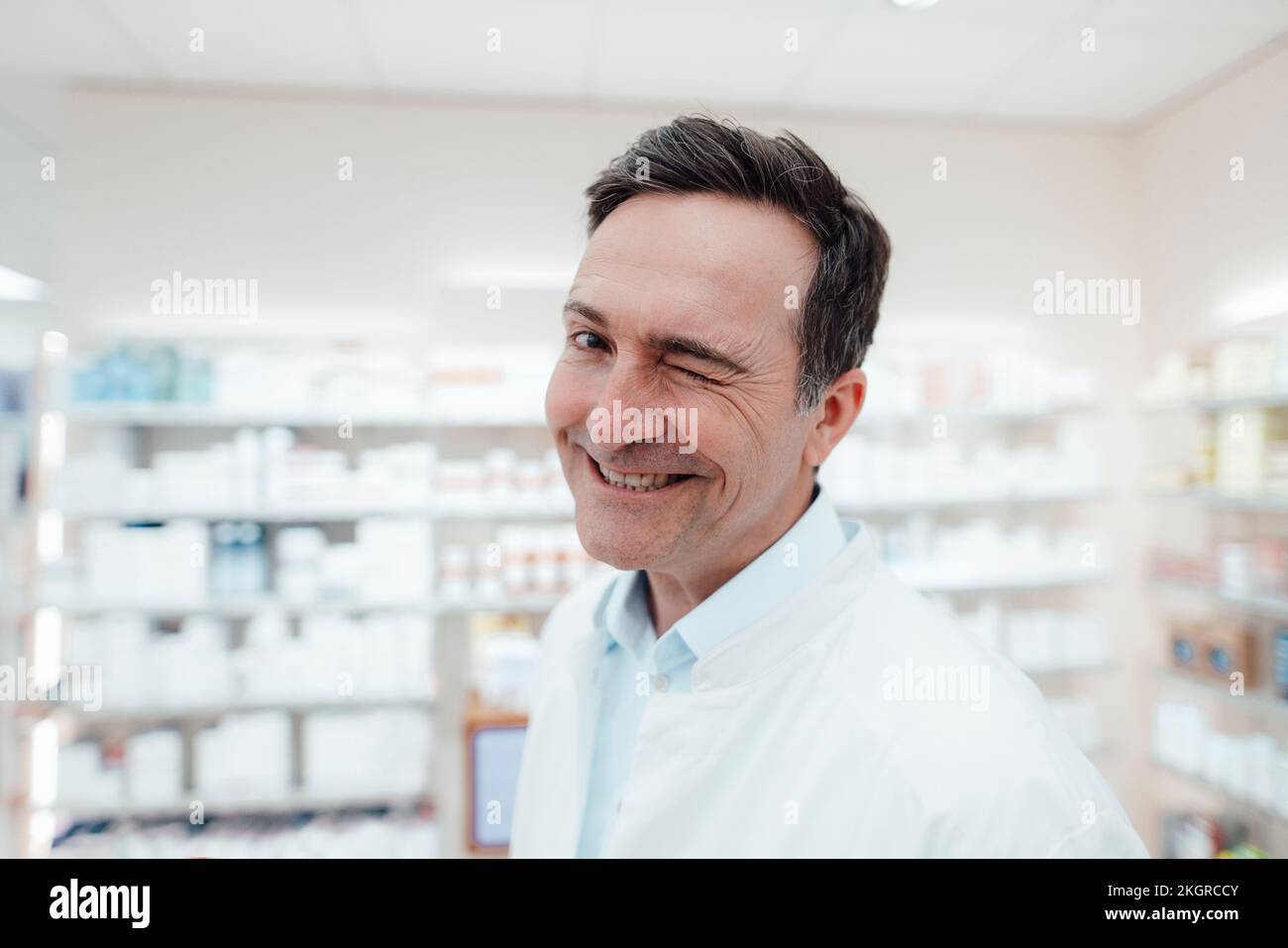 Happy pharmacist in lab coat winking at store Stock Photo - Alamy