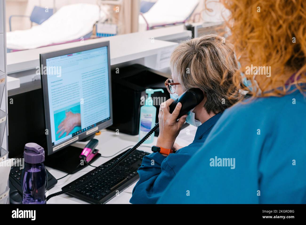 Nurse with colleague talking on telephone and using computer at ...