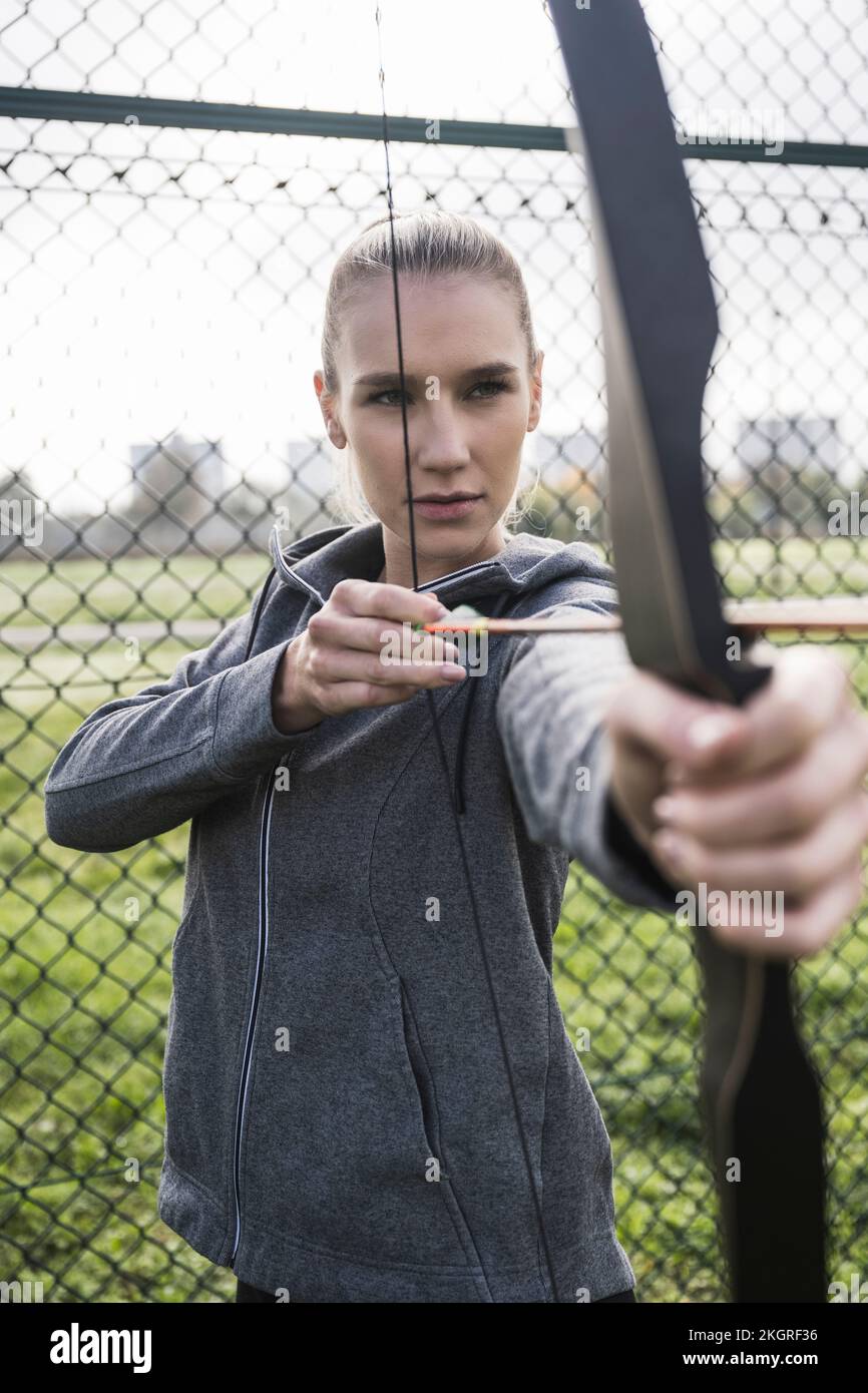 Young sportswoman doing archery in front of fence Stock Photo - Alamy