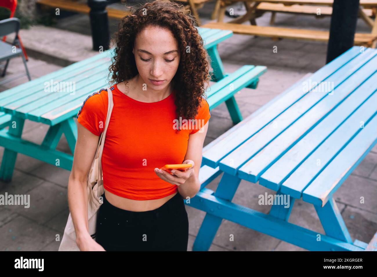 Young woman looking at mobile phone in front of picnic tables Stock ...