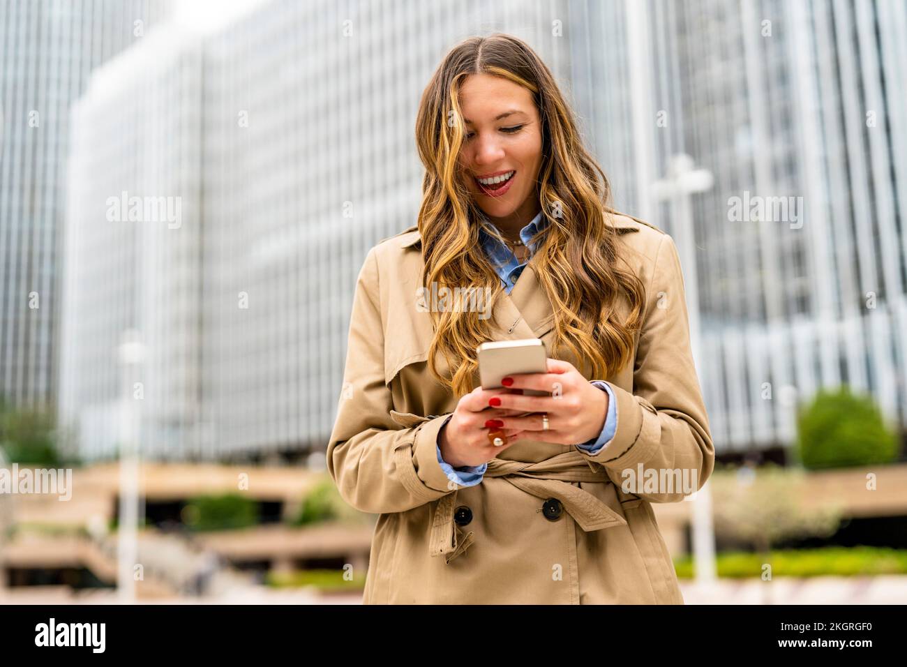 Surprised businesswoman using smart phone in front of office building ...